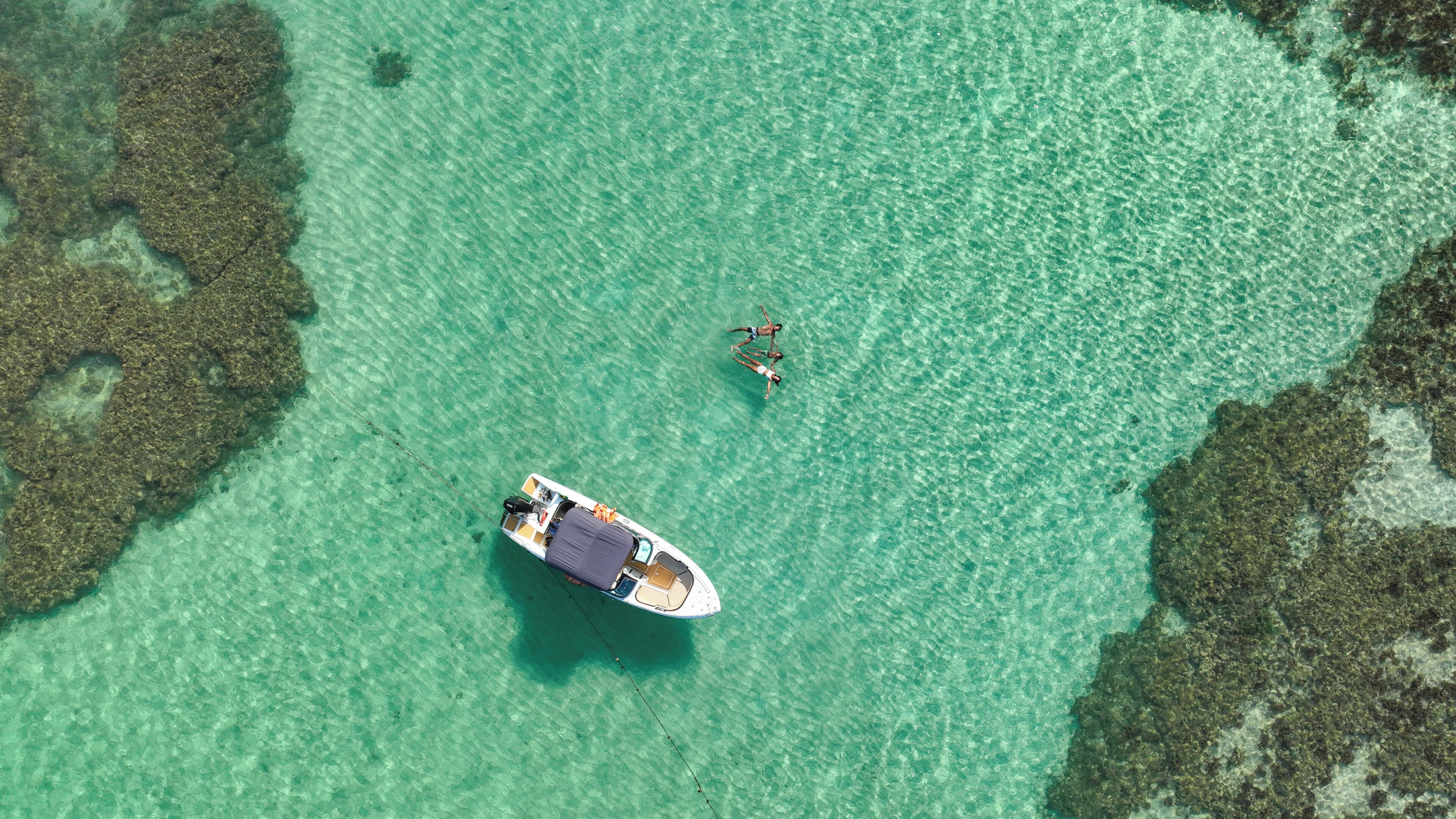 Vista aérea de um barco em águas turquesas cristalinas, com ilhas rochosas ao fundo.