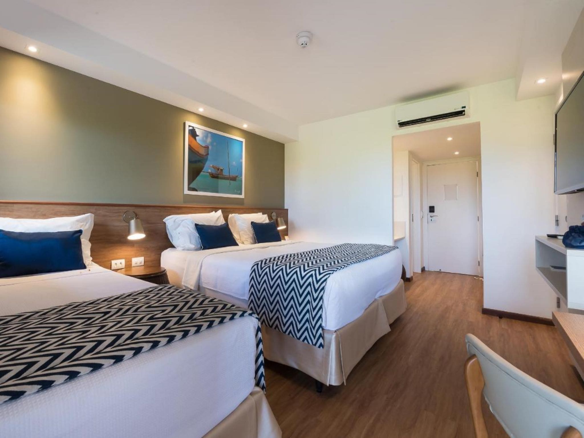Quarto de hotel com duas camas, uma escrivaninha, uma cadeira e uma televisão.