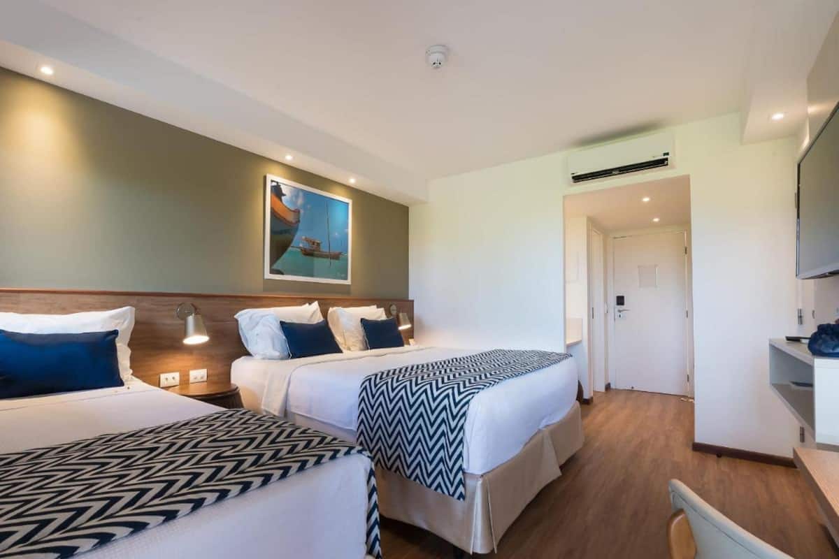 Quarto de hotel com duas camas, uma escrivaninha, uma cadeira e uma televisão.