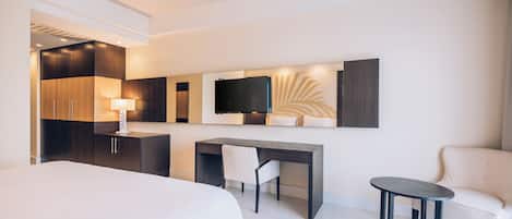 Quarto de hotel moderno com uma cama grande, uma escrivaninha, uma cadeira, uma mesinha e uma televisão fixada na parede.