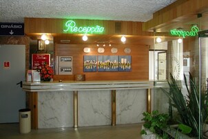 Uma área de recepção com balcão de mármore, um letreiro de neon acima e uma pintura com vista para a cidade na parede.