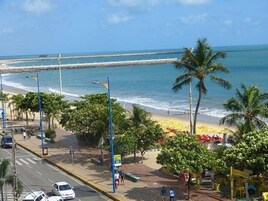 Uma rua à beira-mar com palmeiras, um passeio para pedestres e vista para o oceano.