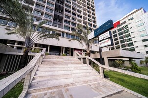 Entrada de hotel com escadaria moderna, palmeiras e uma placa com a inscrição 'Hotel Praia Mar'.