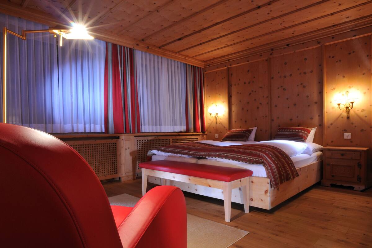 Quarto com painéis de madeira, cama, um banco e duas luminárias fixadas na parede.