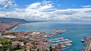 Paisagem costeira com uma marina repleta de barcos, uma torre imponente e uma variedade de edifícios residenciais e comerciais.