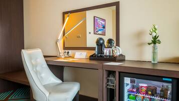 Quarto de hotel com escrivaninha, cadeira, espelho, cafeteira e mini-geladeira.