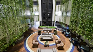 Um amplo átrio interno com área de estar central, rodeado por mesas e cadeiras, e paredes decoradas com plantas pendentes.