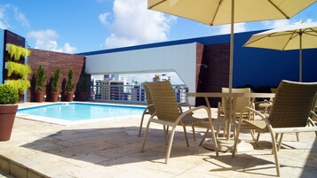 Uma área de piscina no terraço com vista para o horizonte da cidade, cercada por plantas em vasos e móveis de vime.