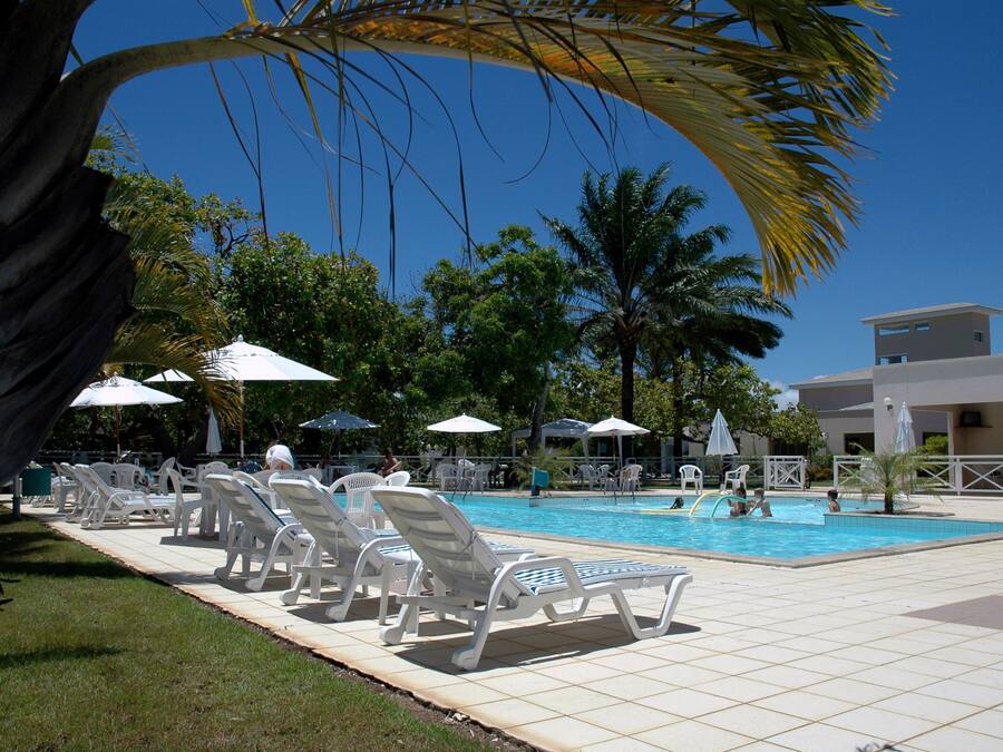 Área à beira da piscina com espreguiçadeiras, guarda-sóis e um céu azul límpido.