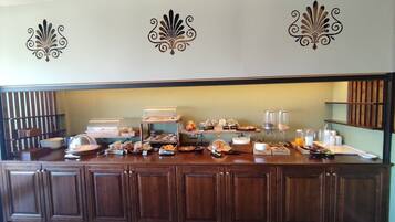 Buffet com diversos alimentos e bebidas, armários de madeira e detalhes decorativos na parede.