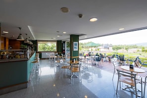 Um café espaçoso com balcão, banquetes e mesas. Possui uma grande janela com vista para o exterior.