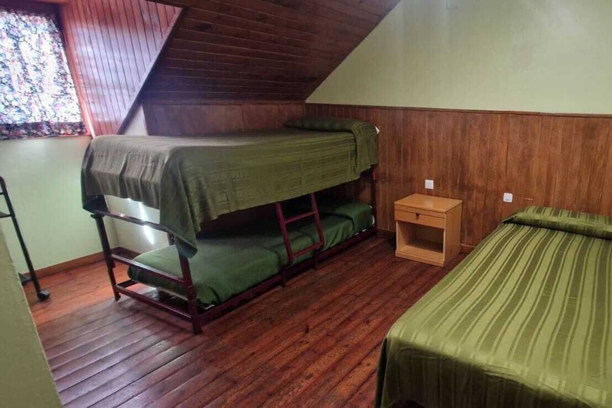 Um quarto de dormitório com duas beliches, uma pequena mesa de cabeceira de madeira e uma janela com cortina florida.