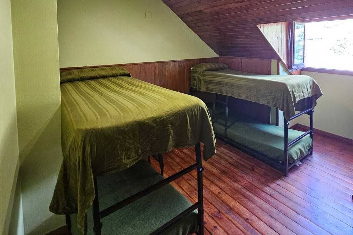 Quarto de estudante com duas camas beliche, soalho de madeira e teto inclinado com claraboia.
