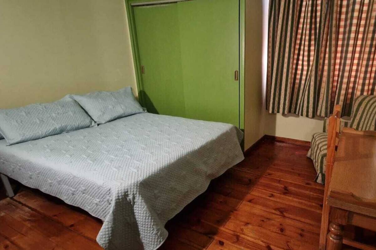 Um quarto com uma cama, uma porta verde, uma mesa de madeira e uma cadeira.