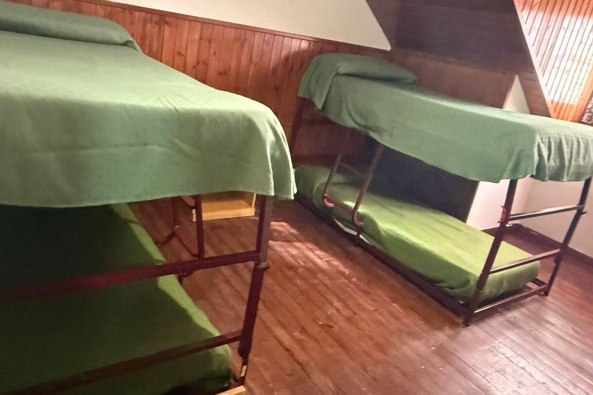 Beliches com cobertores verdes em um quarto com paredes e piso de madeira.