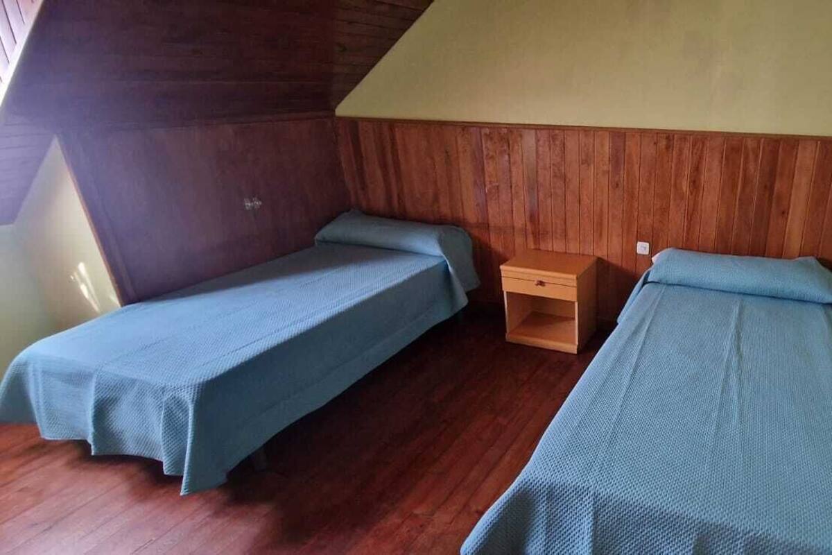 Um quarto pequeno e aconchegante com duas camas de solteiro, paredes de madeira e teto inclinado.