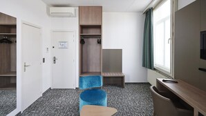 Quarto de hotel com guarda-roupa, escrivaninha, cadeira e janela.