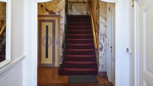 Um hall imponente com piso de mármore, escada revestida de carpete vermelho e detalhes dourados elaborados no teto.