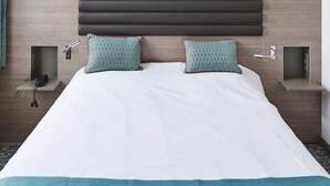 Quarto de hotel com uma cama grande, duas almofadas, mesa de cabeceira com abajur e telefone.