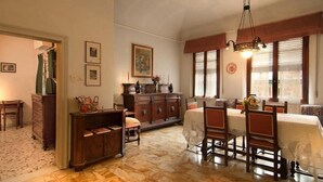 Uma área de refeições com uma mesa posta para quatro pessoas, ladeada por cadeiras, um armário de madeira e um lustre.