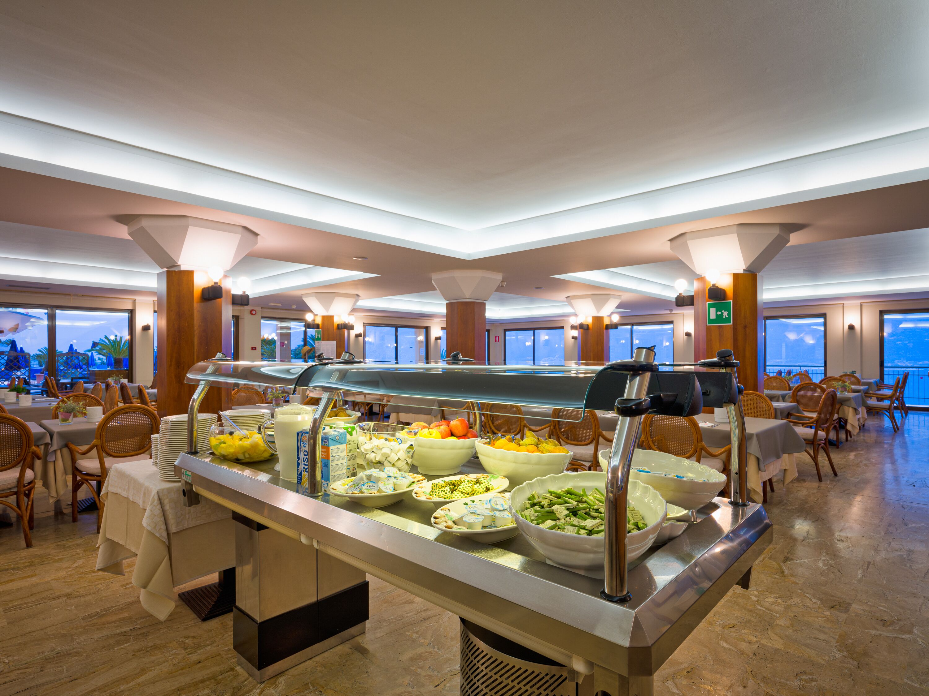 Uma área de buffet com diversos alimentos, mesas e cadeiras dispostas para refeições.