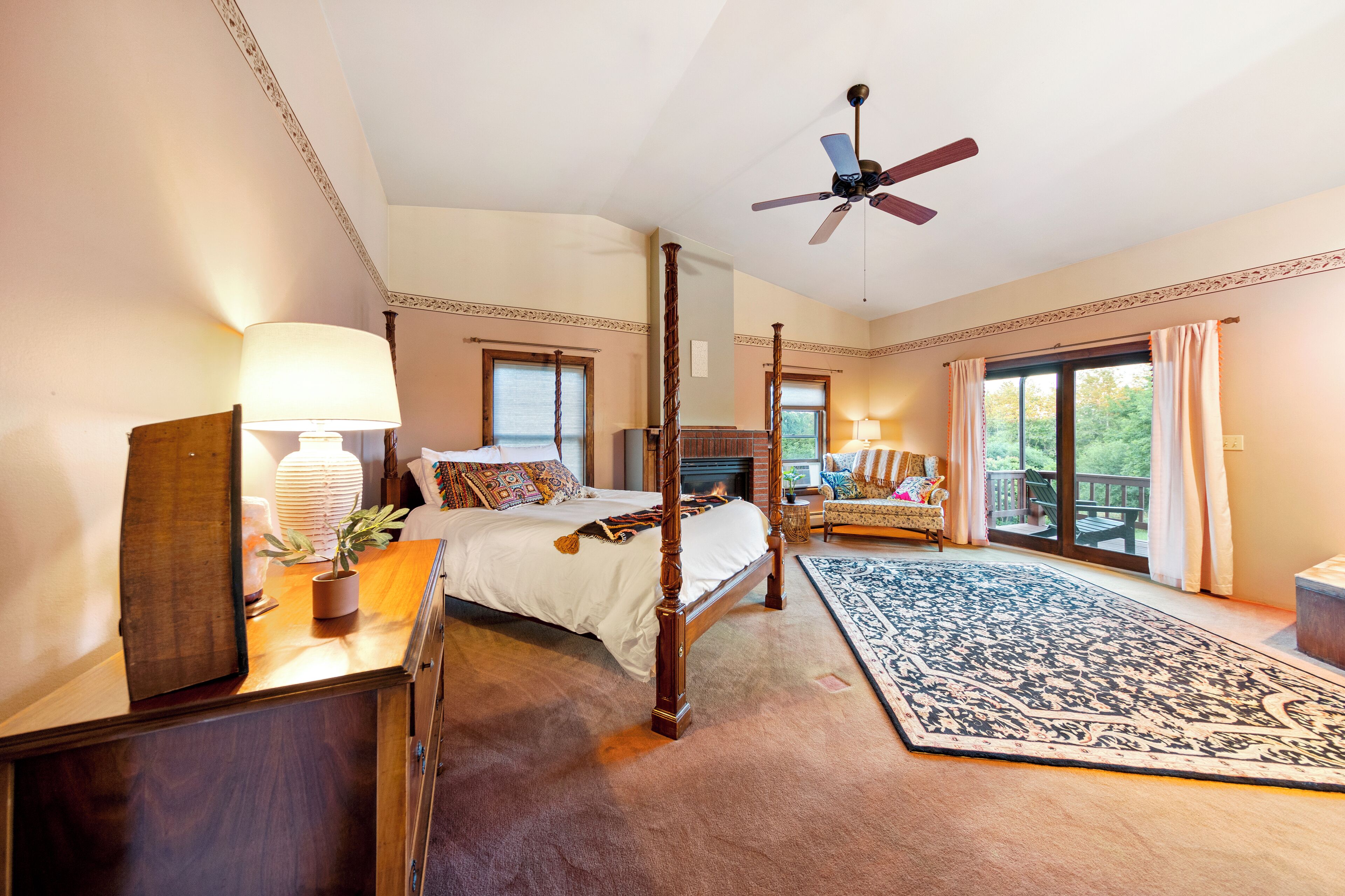 Um quarto espaçoso com uma cama grande, um ventilador de teto, uma lareira e vista para o exterior através de uma porta de correr de vidro.
