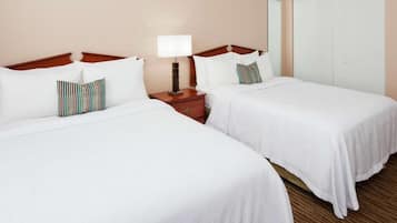 Quarto de hotel com duas camas, uma mesa de cabeceira com abajur, um guarda-roupa e um espelho.
