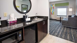 Quarto de hotel moderno com cozinha, incluindo micro-ondas, pia e bancada com amenities de higiene pessoal.