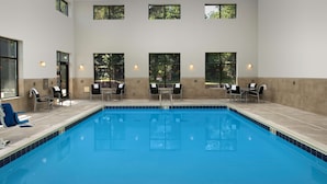 Piscina com cadeiras e mesas, janelas amplas e piso revestido.
