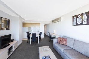 Uma sala de estar moderna com uma televisão de tela plana, um sofá, uma mesa de centro e um espaço de jantar com cadeiras e uma mesa.