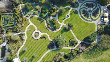Vista aérea de um jardim ajardinado com caminhos sinuosos, um elemento circular central e várias áreas verdes.