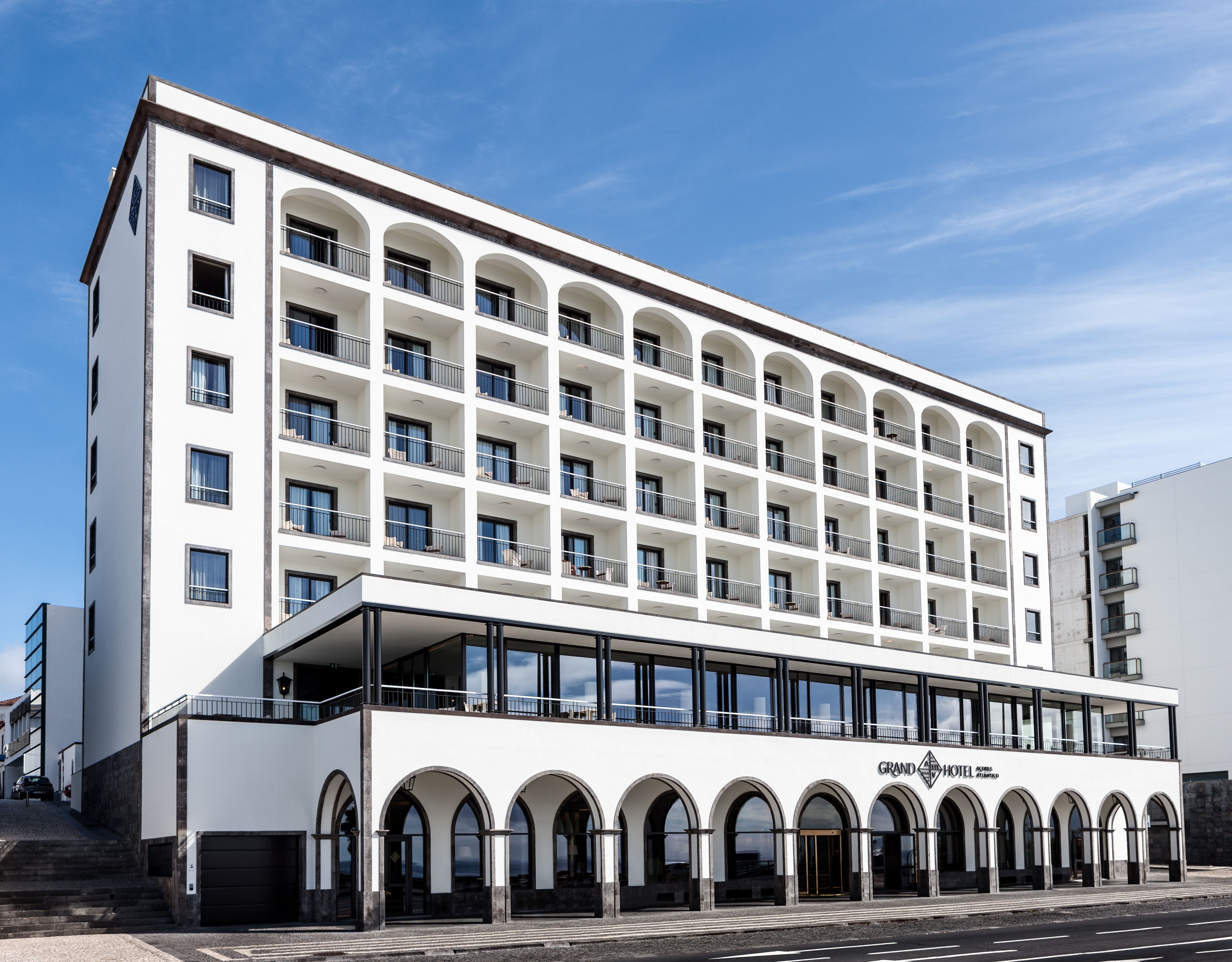 Um hotel moderno com fachada branca, várias varandas e uma entrada imponente com janelas em arco.