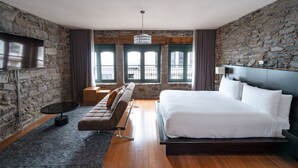 Quarto moderno com parede de pedra, uma cama grande, sofá e televisão.