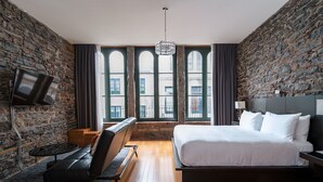 Quarto moderno com cama grande, um banco, televisão e parede de pedra.