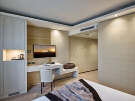 Quarto de hotel moderno com cama, escrivaninha, cadeira, televisão e guarda-roupa.