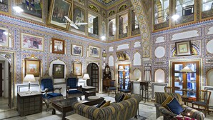 Um interior ricamente decorado, com paredes ornamentadas, vários espaços de estar e um candelabro.
