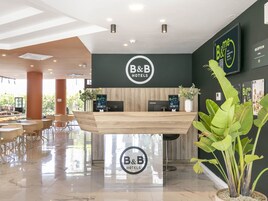 Uma receção de hotel B&B com design moderno, uma estação de check-in digital e uma área de receção.
