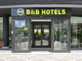 Exterior do B&B Hotels com entrada de vidro e área de estacionamento visível.