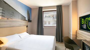 Quarto de hotel com uma cama grande, uma mesa com cadeira, uma TV e um mural de um edifício na parede.