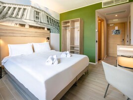 Quarto de hotel com cama, guarda-roupa, espelho e uma parede verde decorativa.
