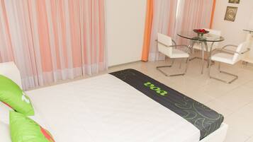 Quarto de hotel com cama, uma mesinha com cadeiras e vista para o exterior através de cortinas finas.