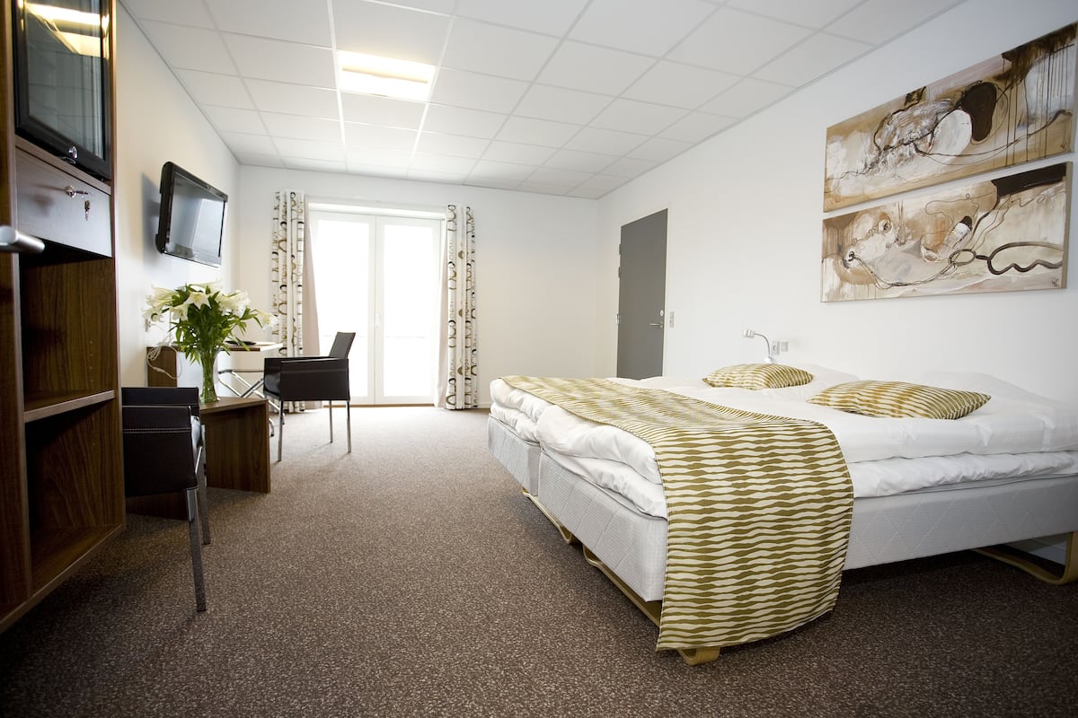 Quarto de hotel com cama, escrivaninha, cadeira, televisão e obras de arte nas paredes.