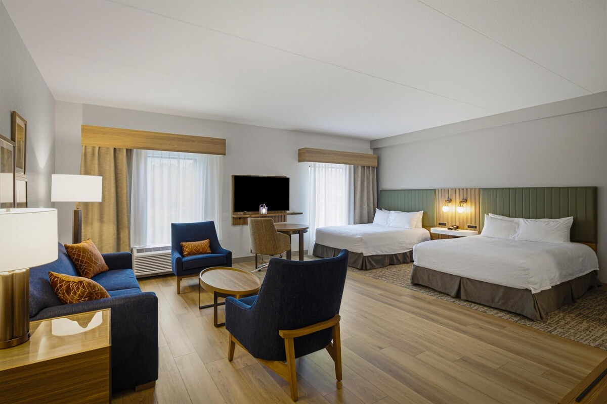 Quarto de hotel com cama, dois sofás, uma televisão e uma escrivaninha.