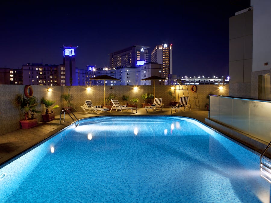Piscina com espreguiçadeiras e guarda-sóis, rodeada por plantas em vasos.