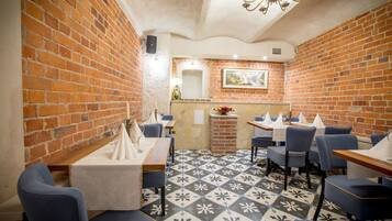 Restaurante com paredes de tijolo, cadeiras azuis e ladrilhos estampados. Mesas montadas com toalhas e guardanapos brancos.