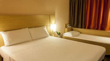 Quarto de hotel com uma cama grande, mesa de cabeceira com abajur e janela com cortinas.