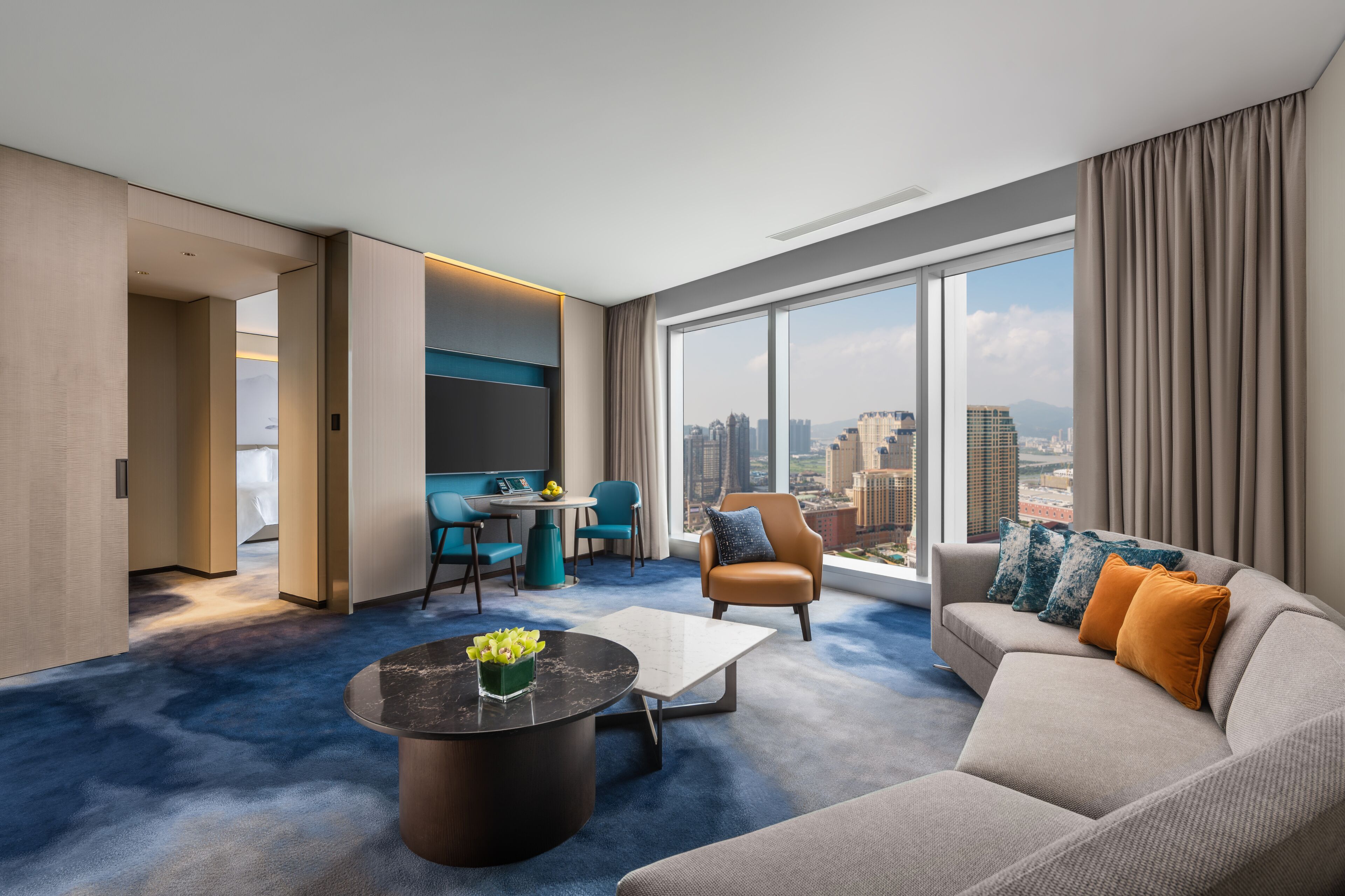Quarto de hotel moderno com uma janela grande, um sofá, uma mesa de centro e um espaço de refeições.