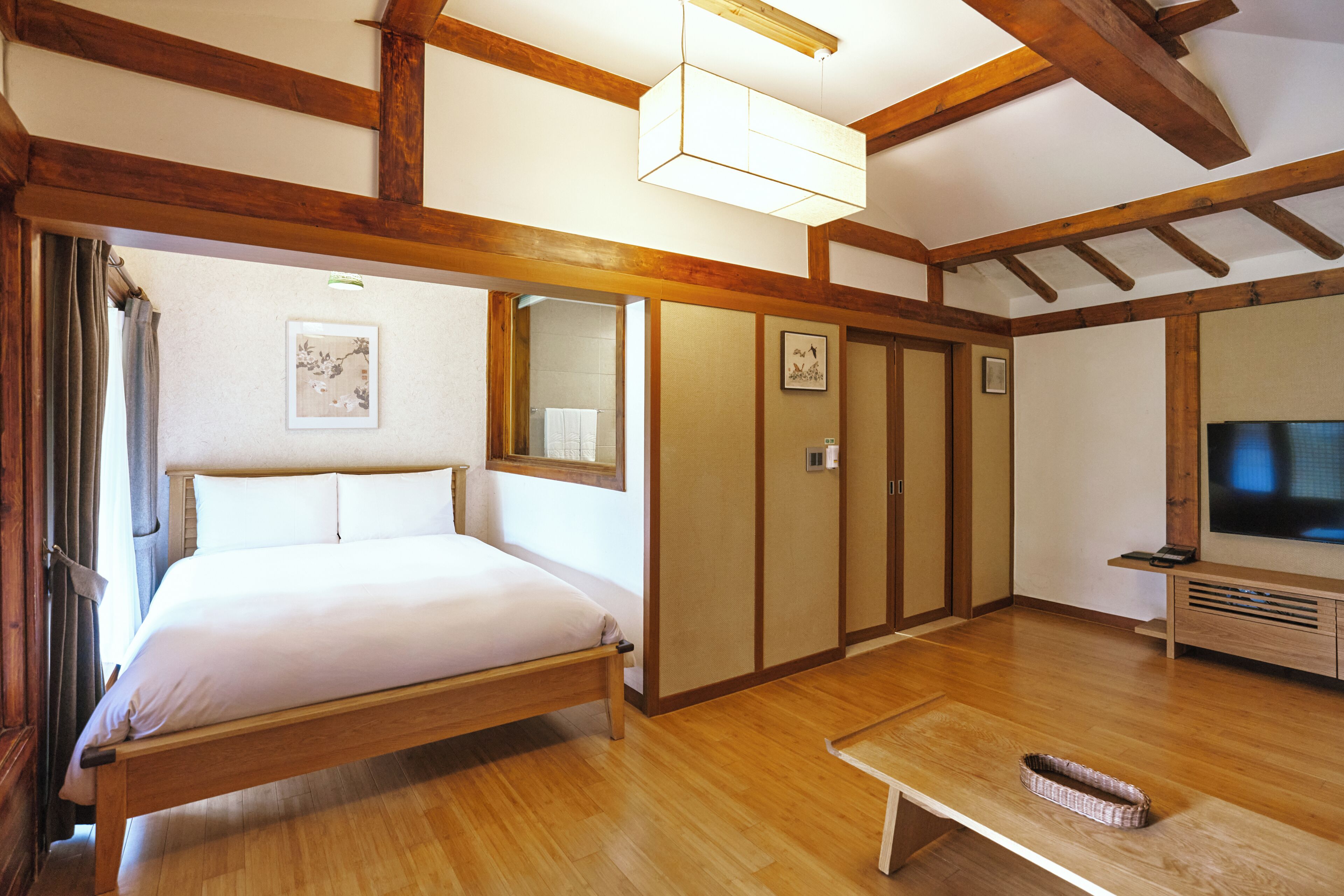 Quarto com cama, vigas de madeira, televisão e uma pequena mesa.
