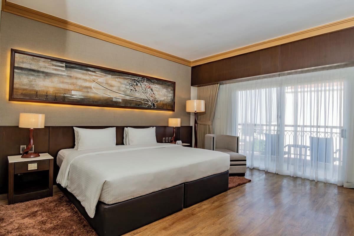 Um quarto de hotel espaçoso com uma cama grande, duas mesas de cabeceira, uma cadeira e uma varanda com cortinas.