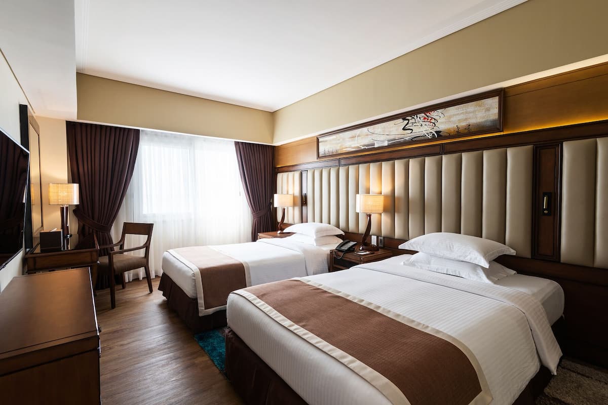 Quarto de hotel com duas camas, uma escrivaninha, uma cadeira e uma televisão.